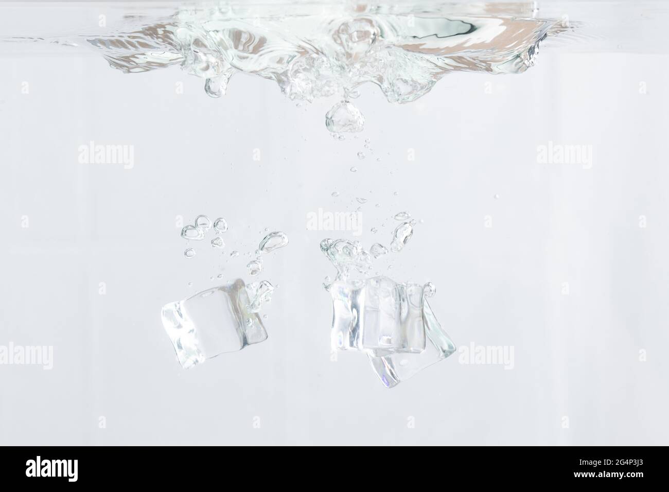 Ice cubes falling into water on white background Stock Photo - Alamy