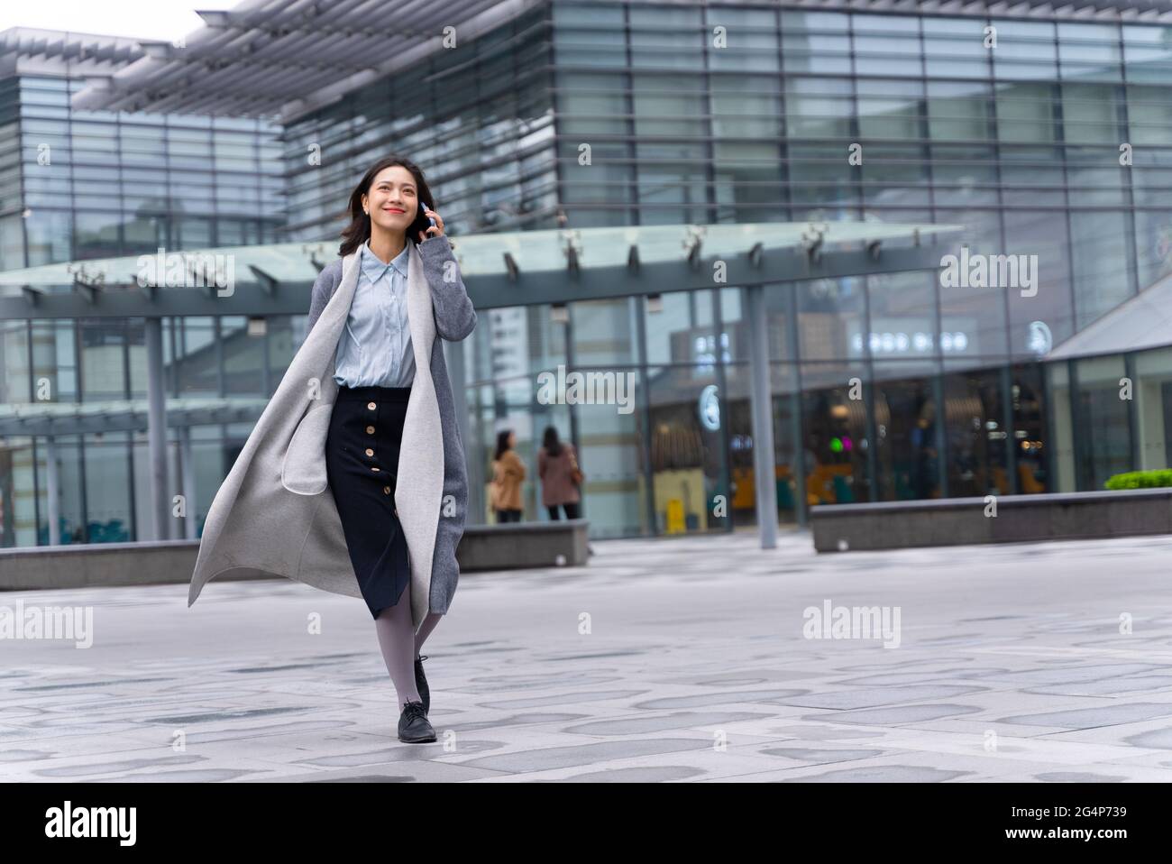 Young beautiful girl walking outside office building using mobile phone ...