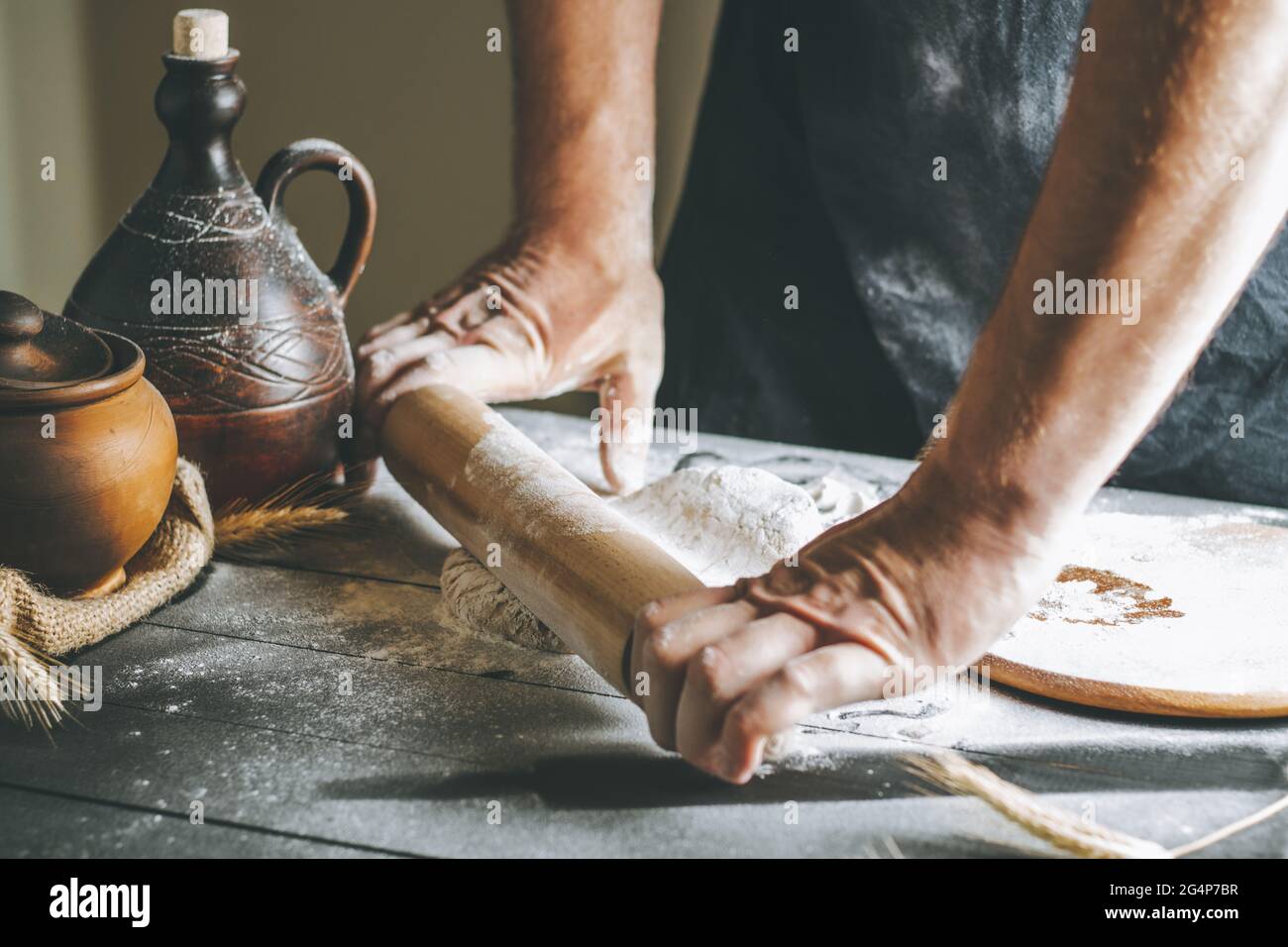Male hands roll dough and flour with rolling pin next to clay pot and ...