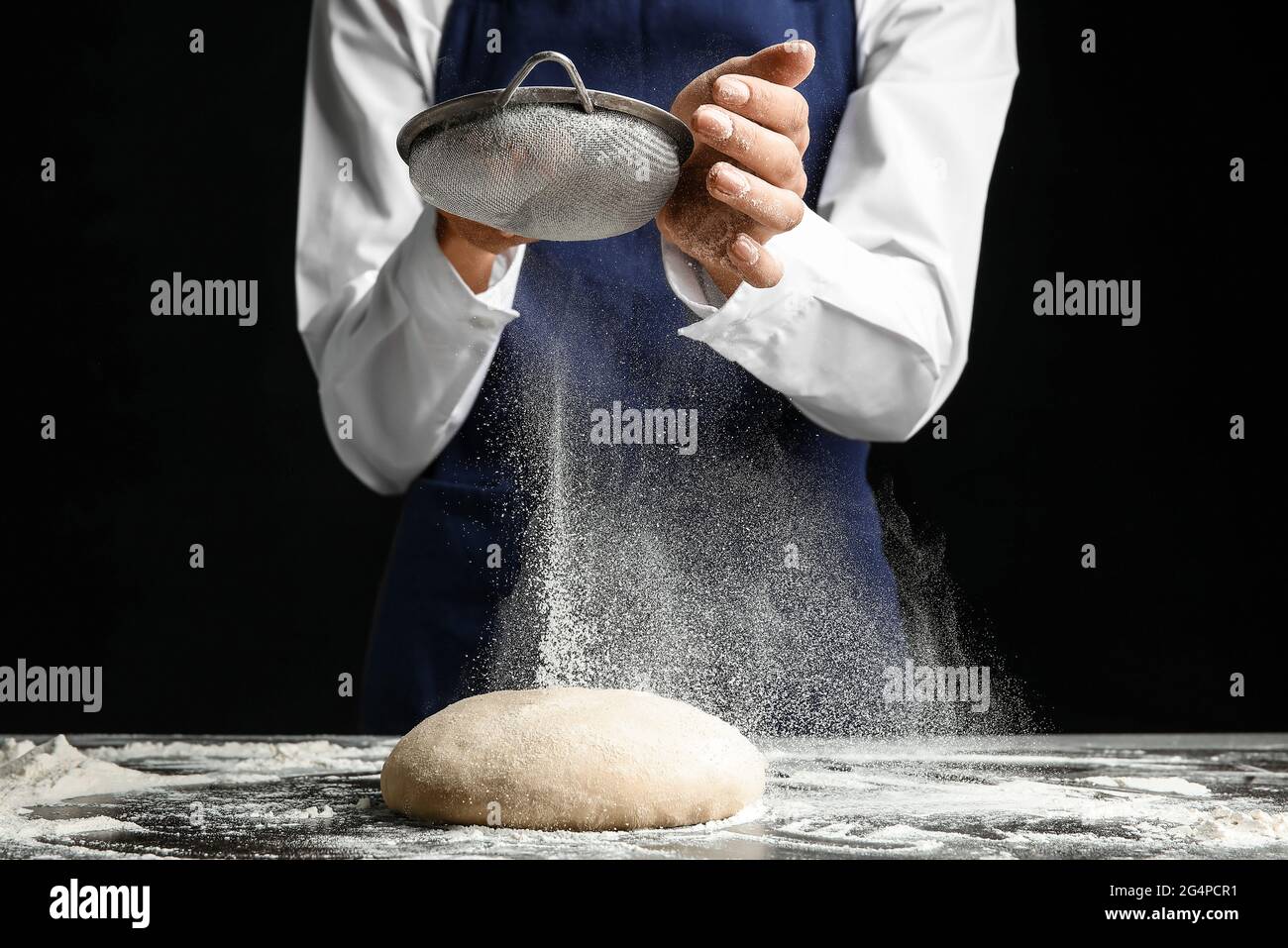 Woman sieving flour on dough on dark background Stock Photo - Alamy