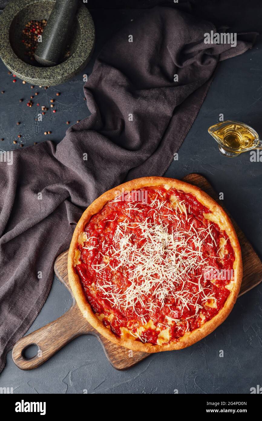 Board with tasty Chicago-style pizza, spices and oil on dark background ...