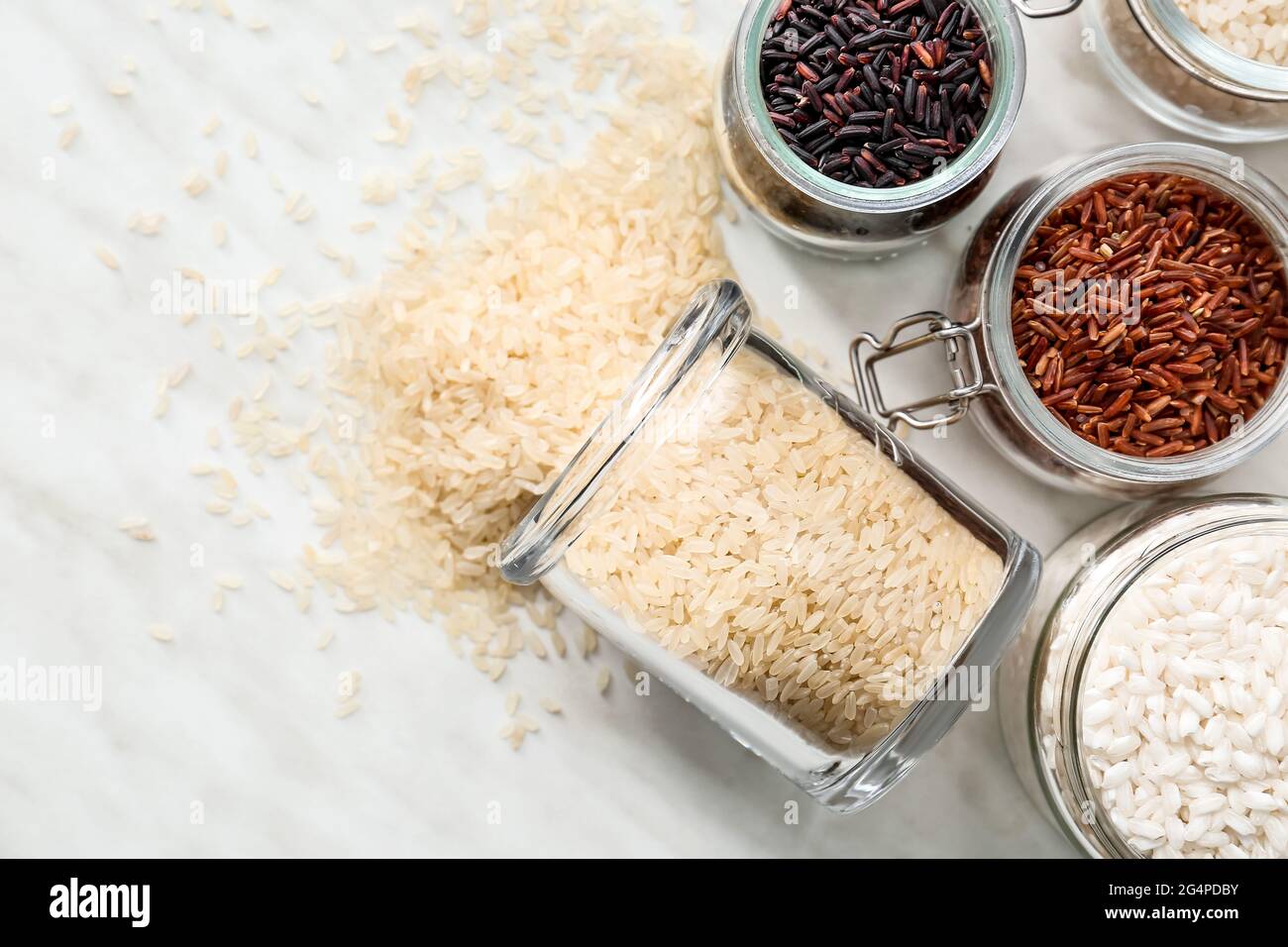 Jars with different types of raw rice on light background Stock Photo ...