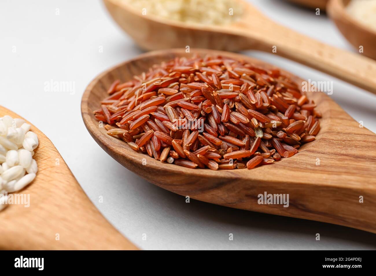 Spoons with different types of raw rice on light background, closeup ...