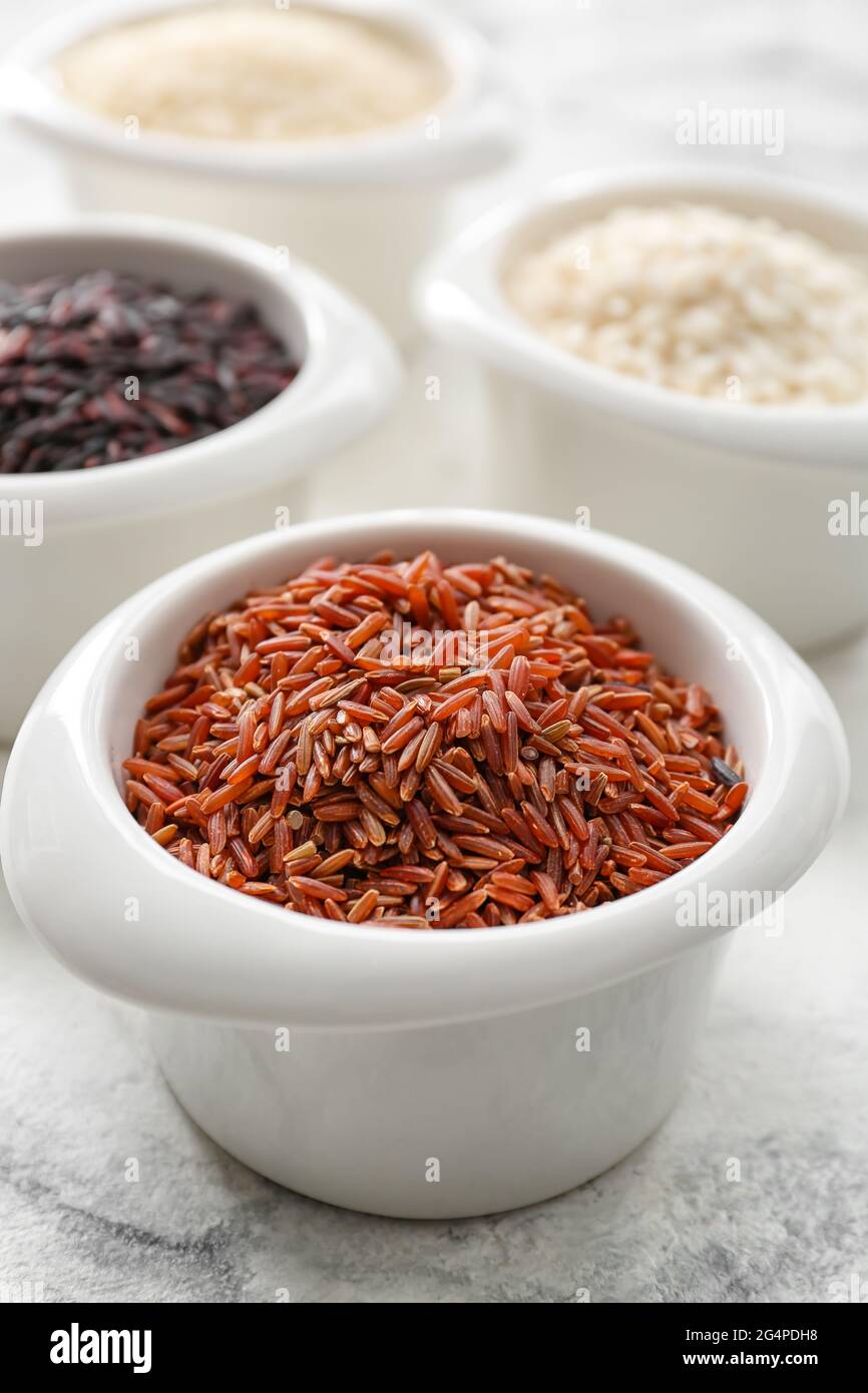 Bowls with different types of raw rice on light background, closeup ...