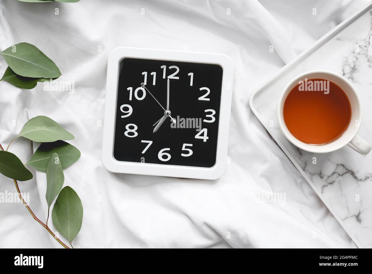 Stylish clock and cup of tea on bed Stock Photo - Alamy