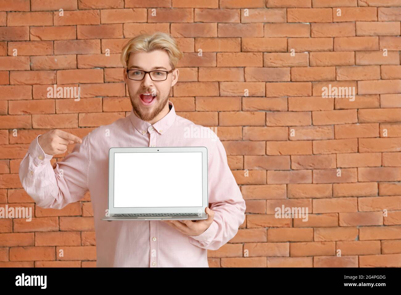 Handsome man pointing at laptop on brick background Stock Photo - Alamy