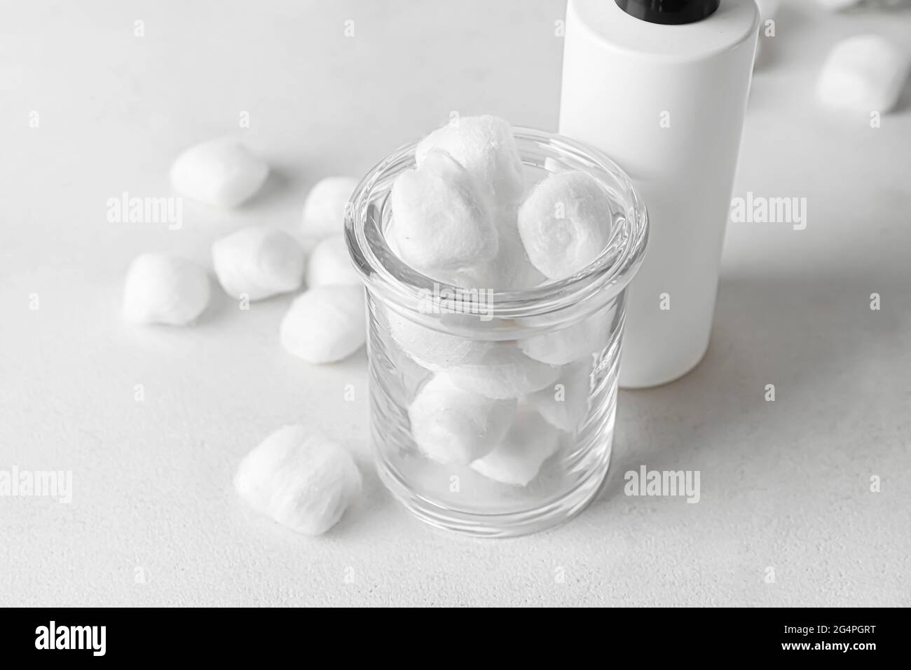 Container with soft cotton wool and cosmetic product on light ...