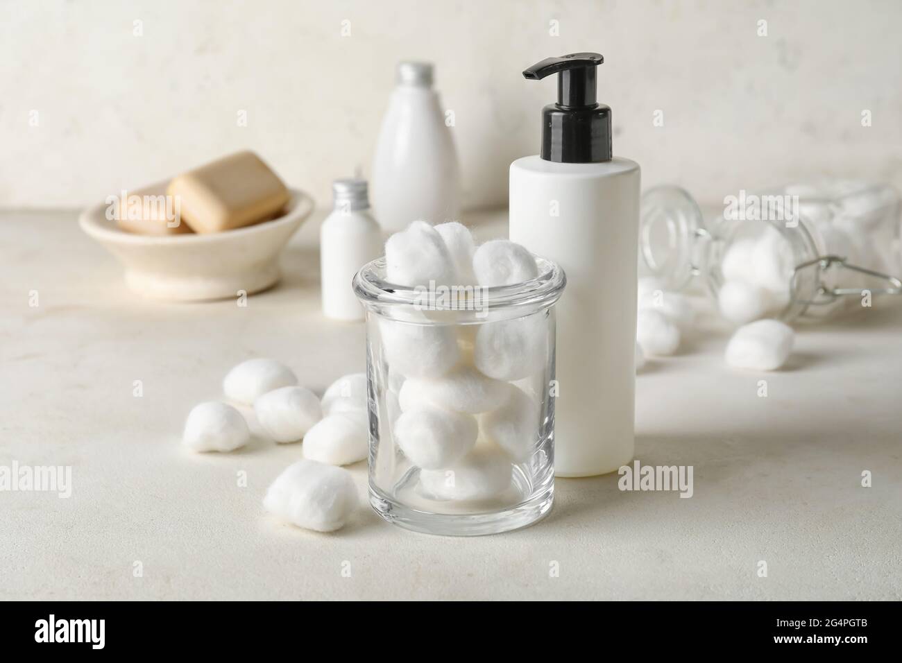 Container with soft cotton wool and cosmetic products on light ...