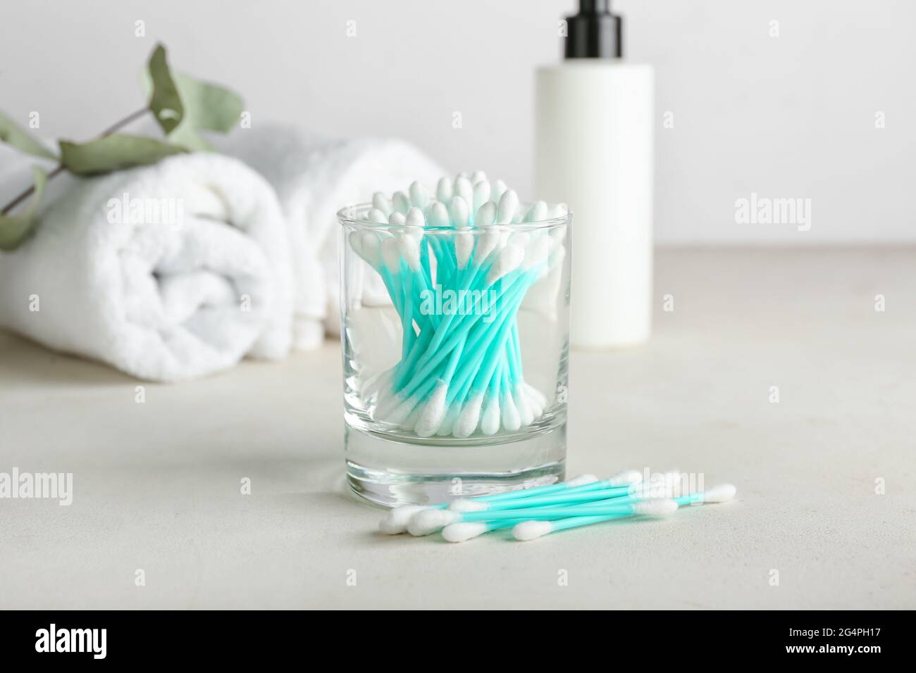 Glass with cotton swabs, bottle of cosmetic product and towels on light ...