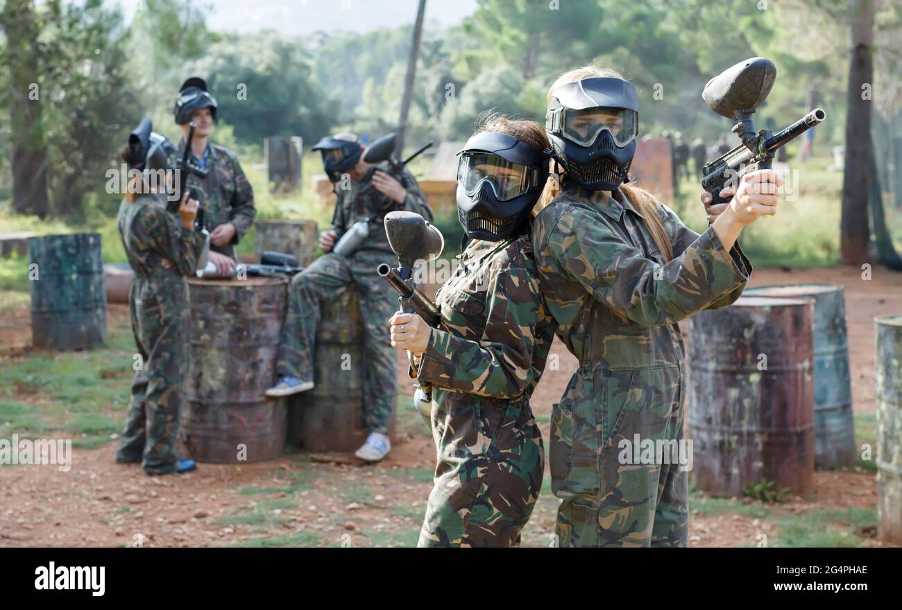 Portrait of happy female paintball players with marker guns outdoors ...