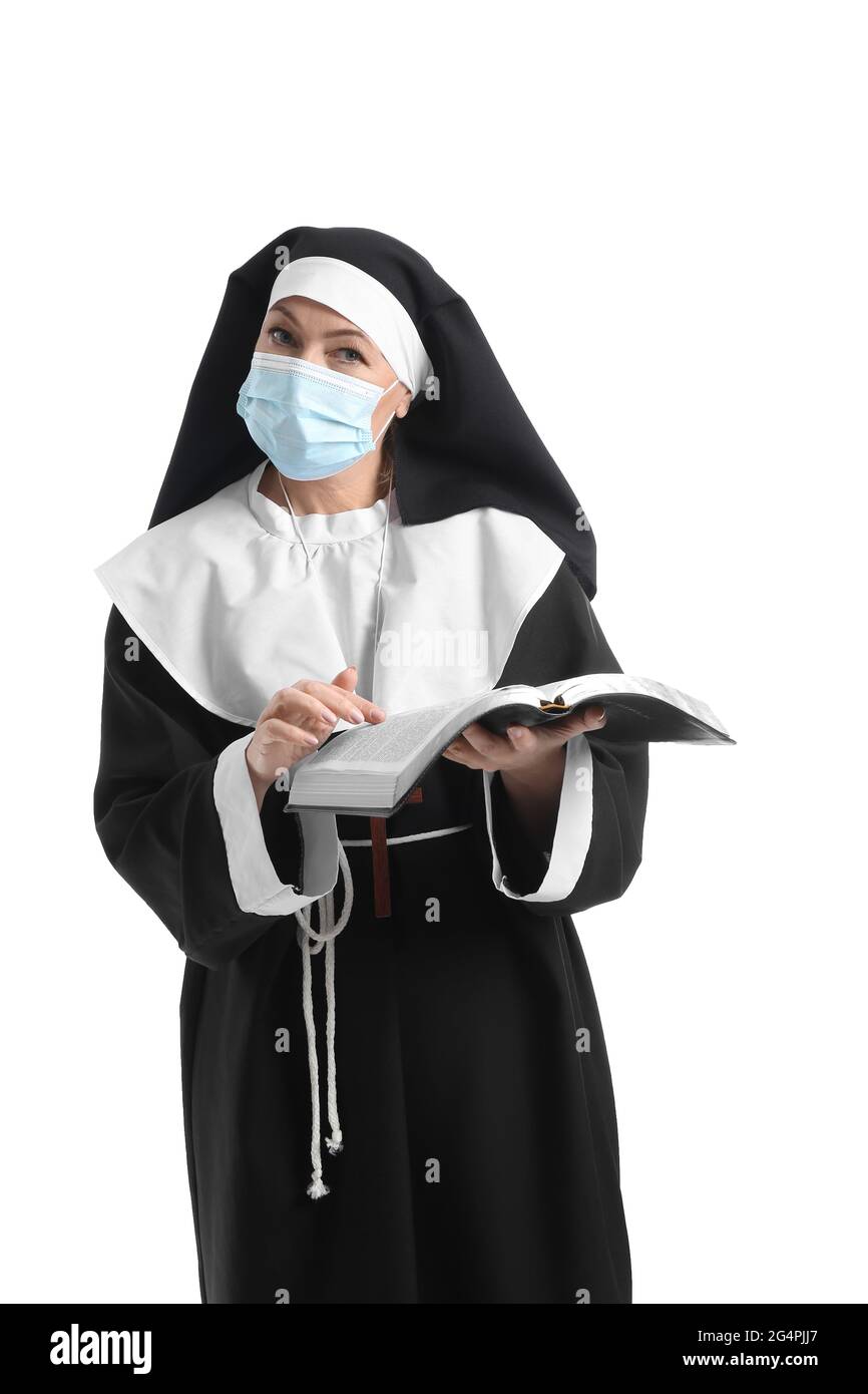 Mature nun in medical mask and with Holy Bible on white background ...
