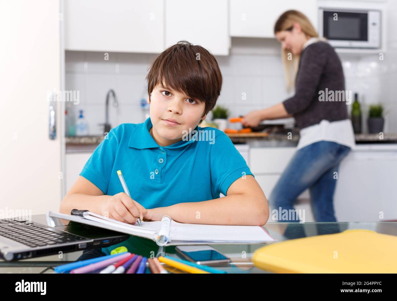 Boy doing homework, mother cooking Stock Photo - Alamy