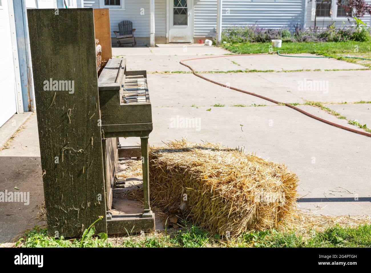 A bale of straw and a decrepit J. A. Starck upright piano sit outside a ...