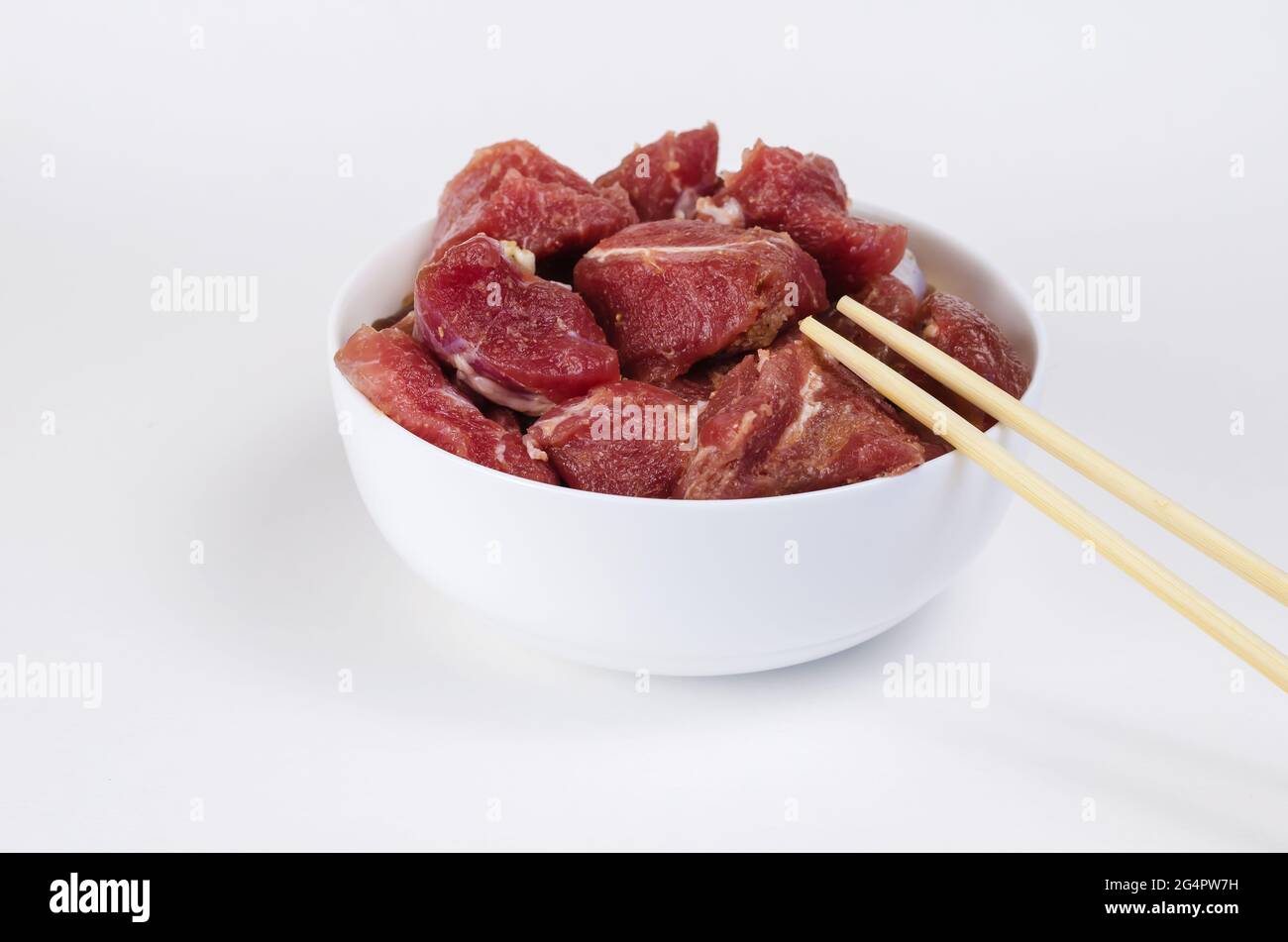 Ceramic bowl with raw marinated meat and bamboo sticks on a white ...