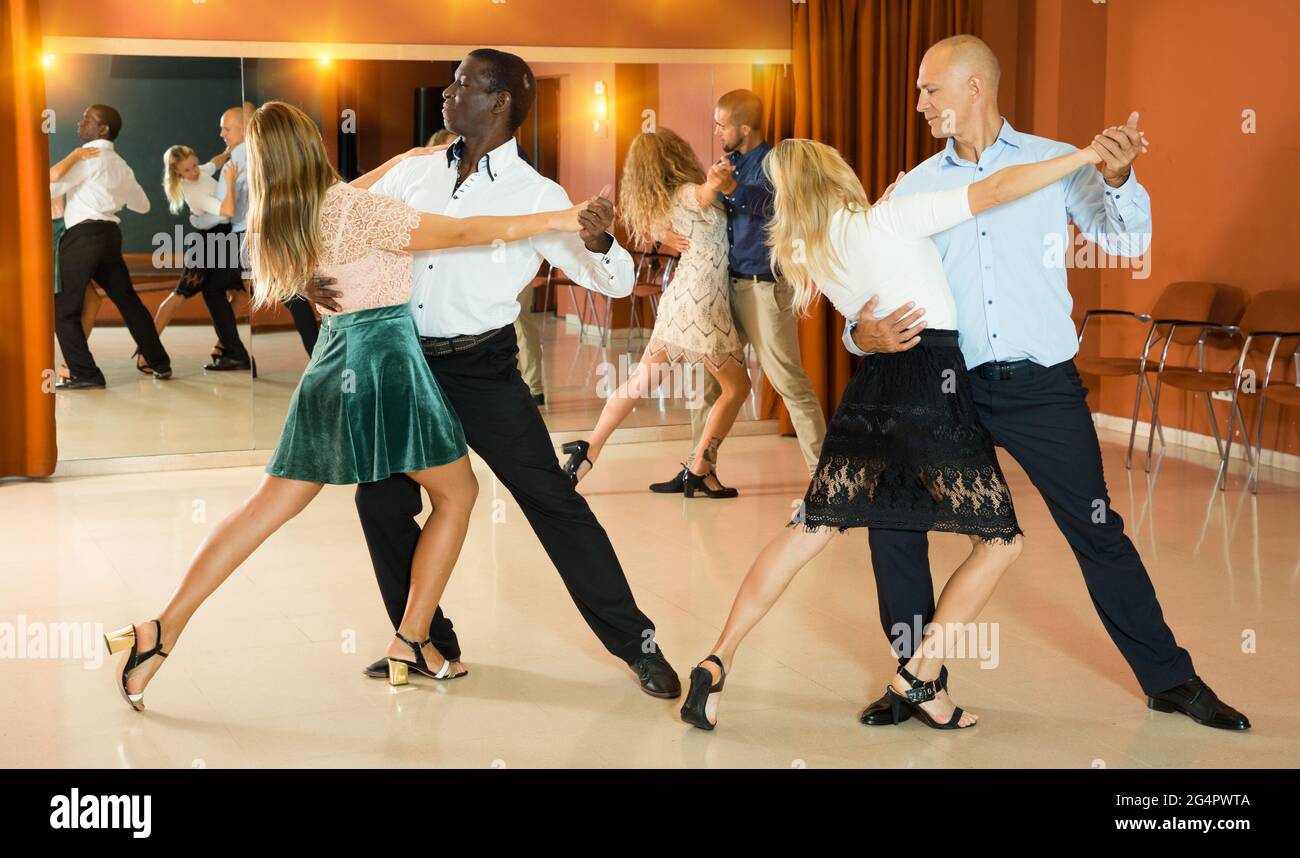 Portrait of positive adult pairs enjoying tango in modern dance hall ...