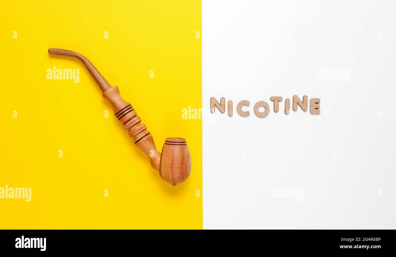 Wooden smoking pipe on white yellow background with word nicotine of ...