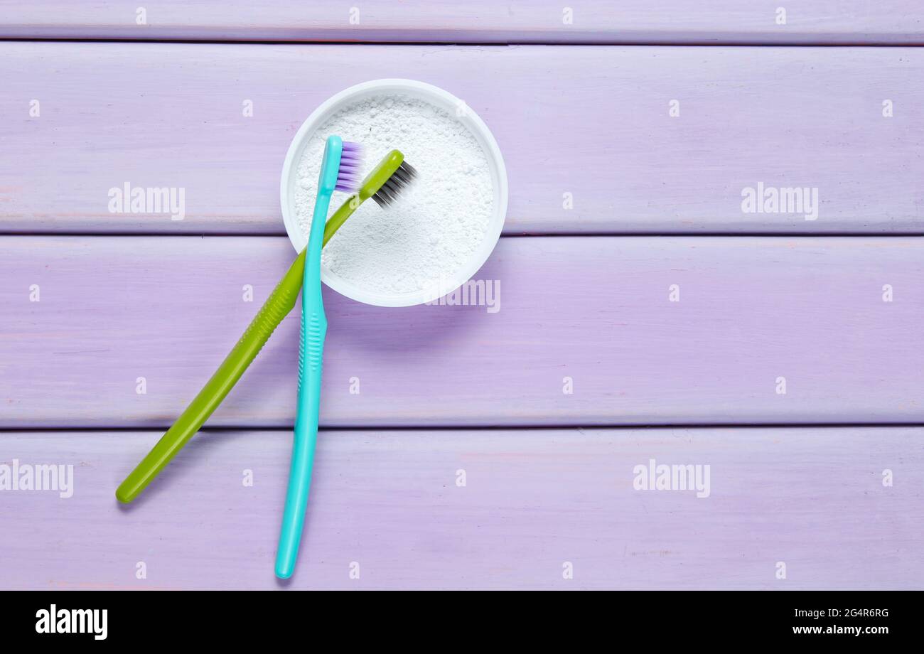 Two toothbrushes, tooth powder on purple wooden background. Minimalism ...