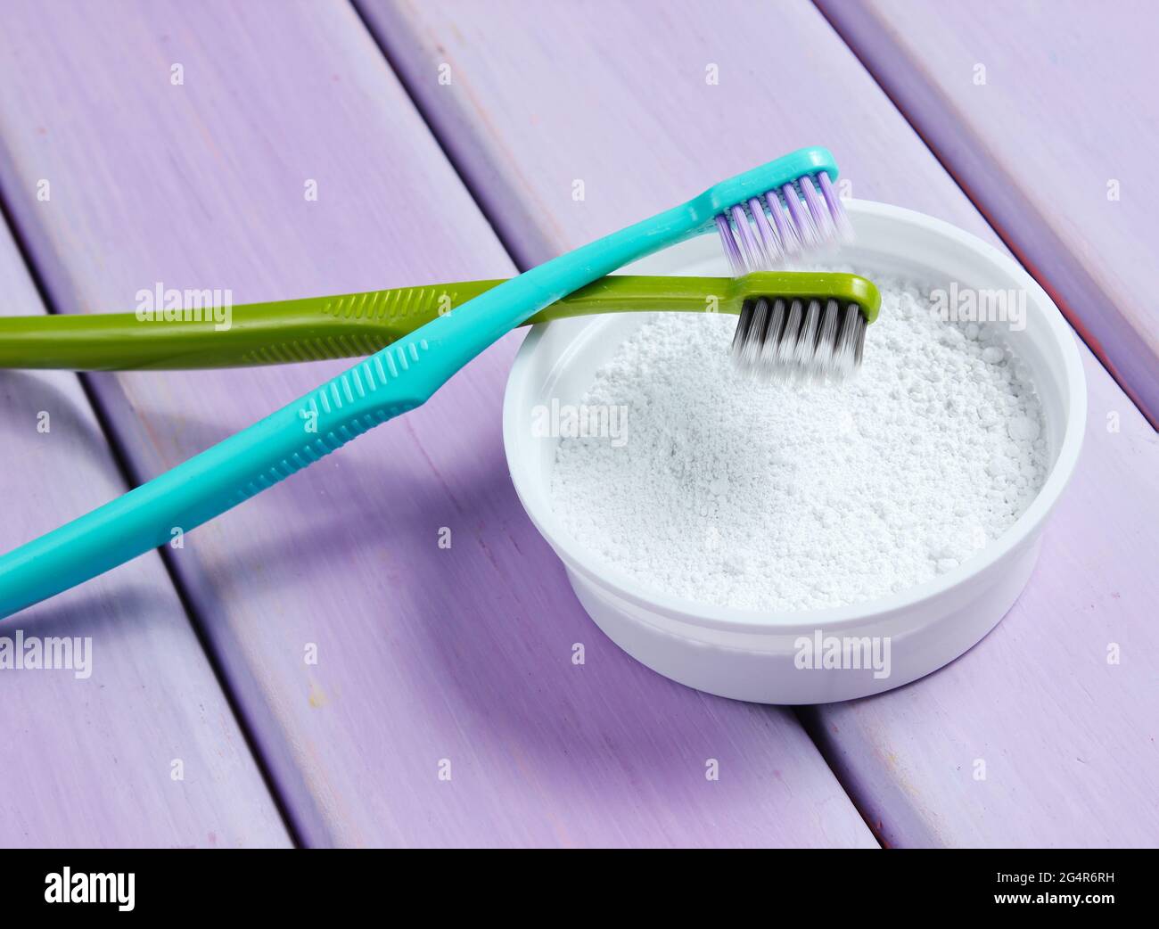 Two toothbrushes, tooth powder on purple wooden background. Minimalism ...