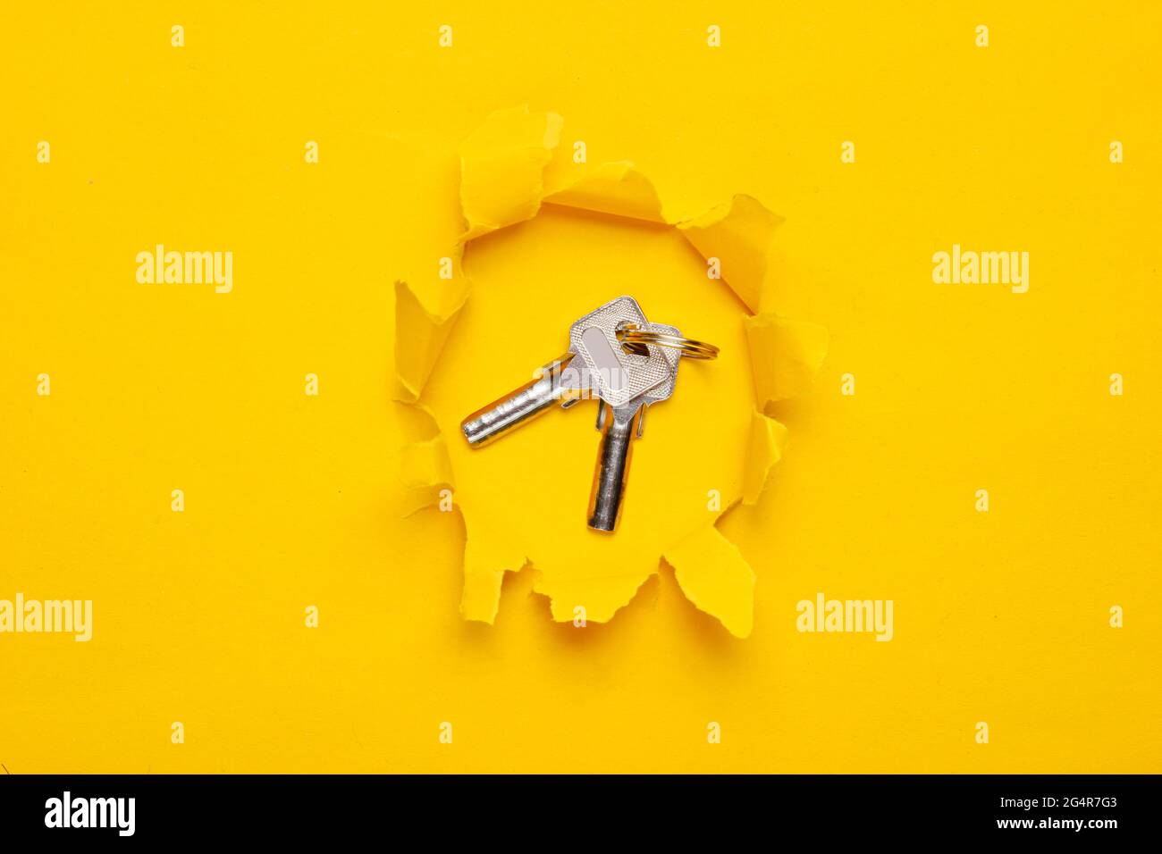 Bunch of metal keys through a torn hole on a yellow paper background ...