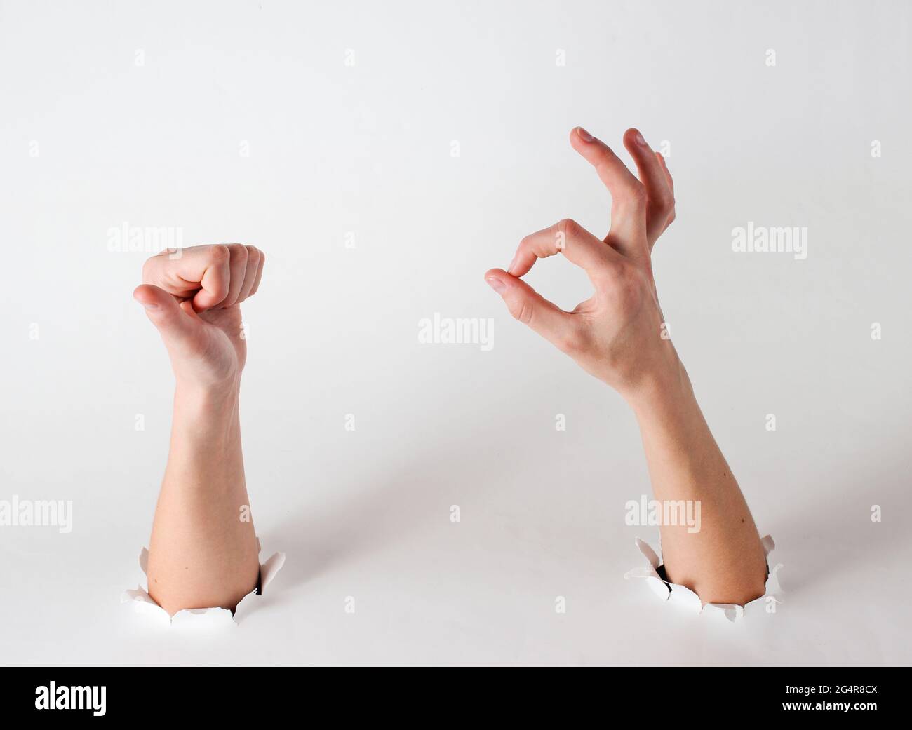 Female hands show thumb up and ok symbol through torn holes of white ...