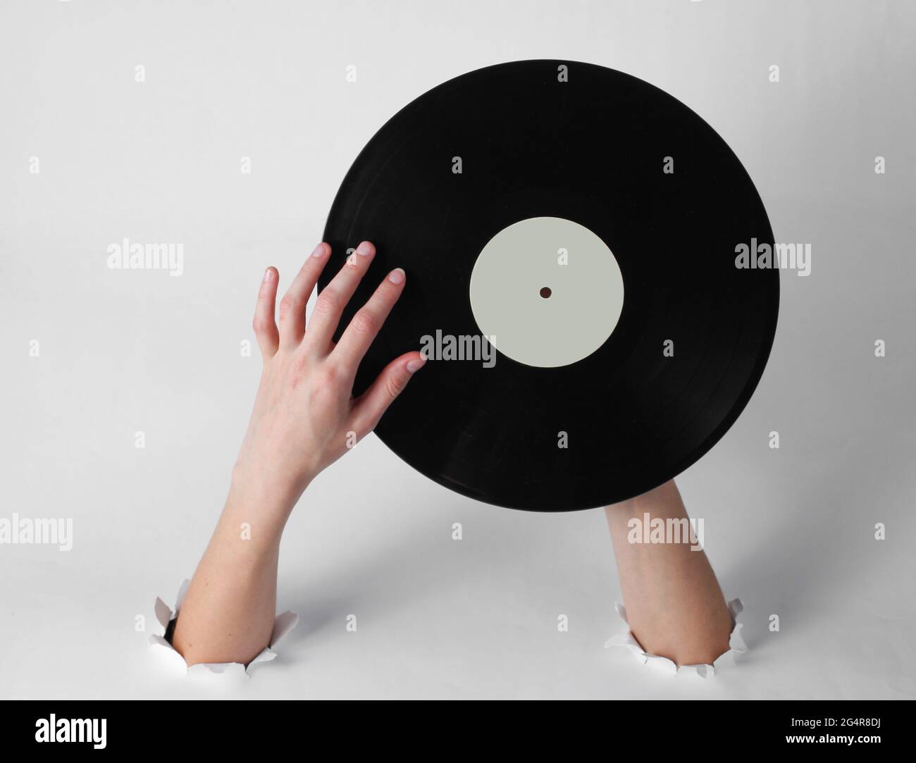 Female hands rotates a vinyl record through the torn holes of a white ...