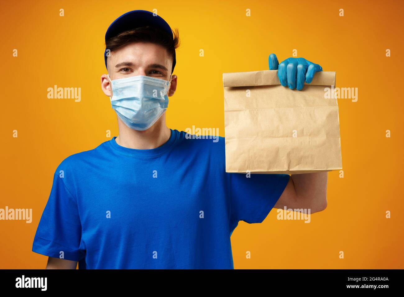 Young delivery man in face mask and gloves holding food delivery parcel ...