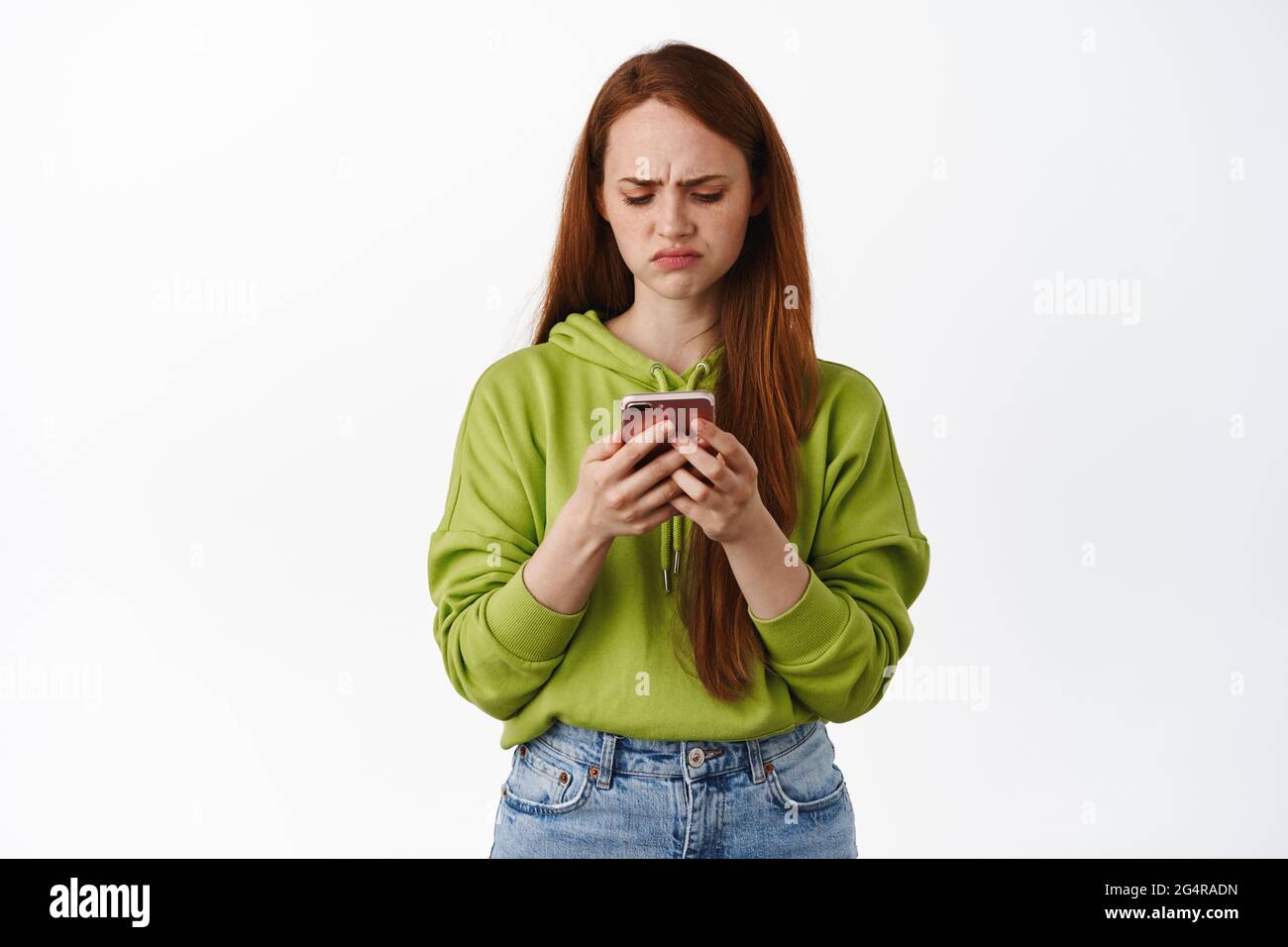 Sad and disappointed ginger teen girl looking upset at her phone ...