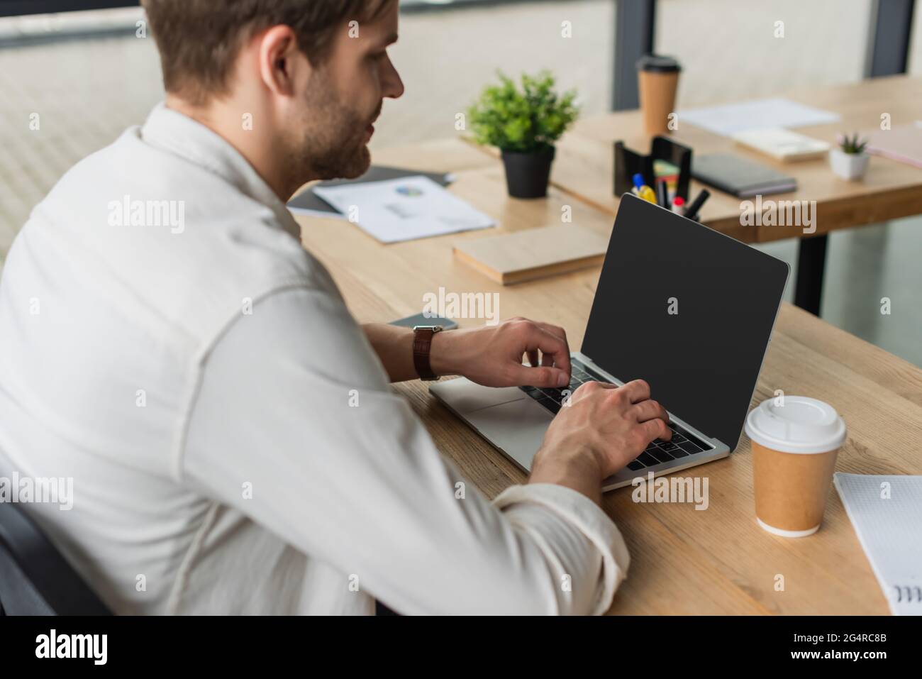 young man sitting at desk and typing on laptop with blank screen in ...