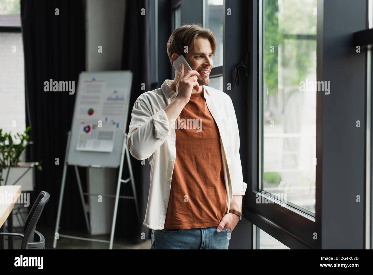 smiling young man talking on cellphone near flip chart with graphs and ...