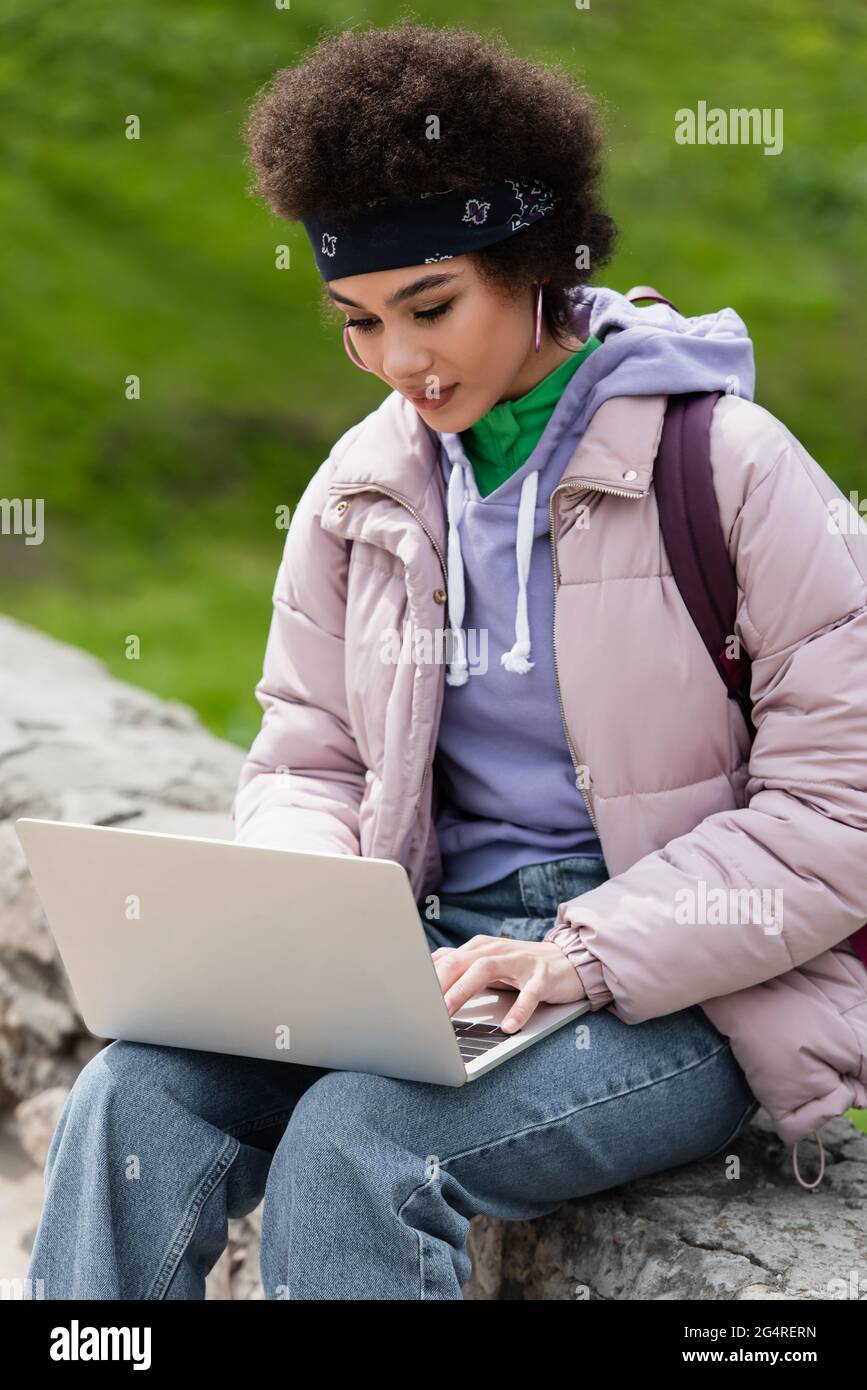 African american teleworker using laptop on parapet in park Stock Photo ...