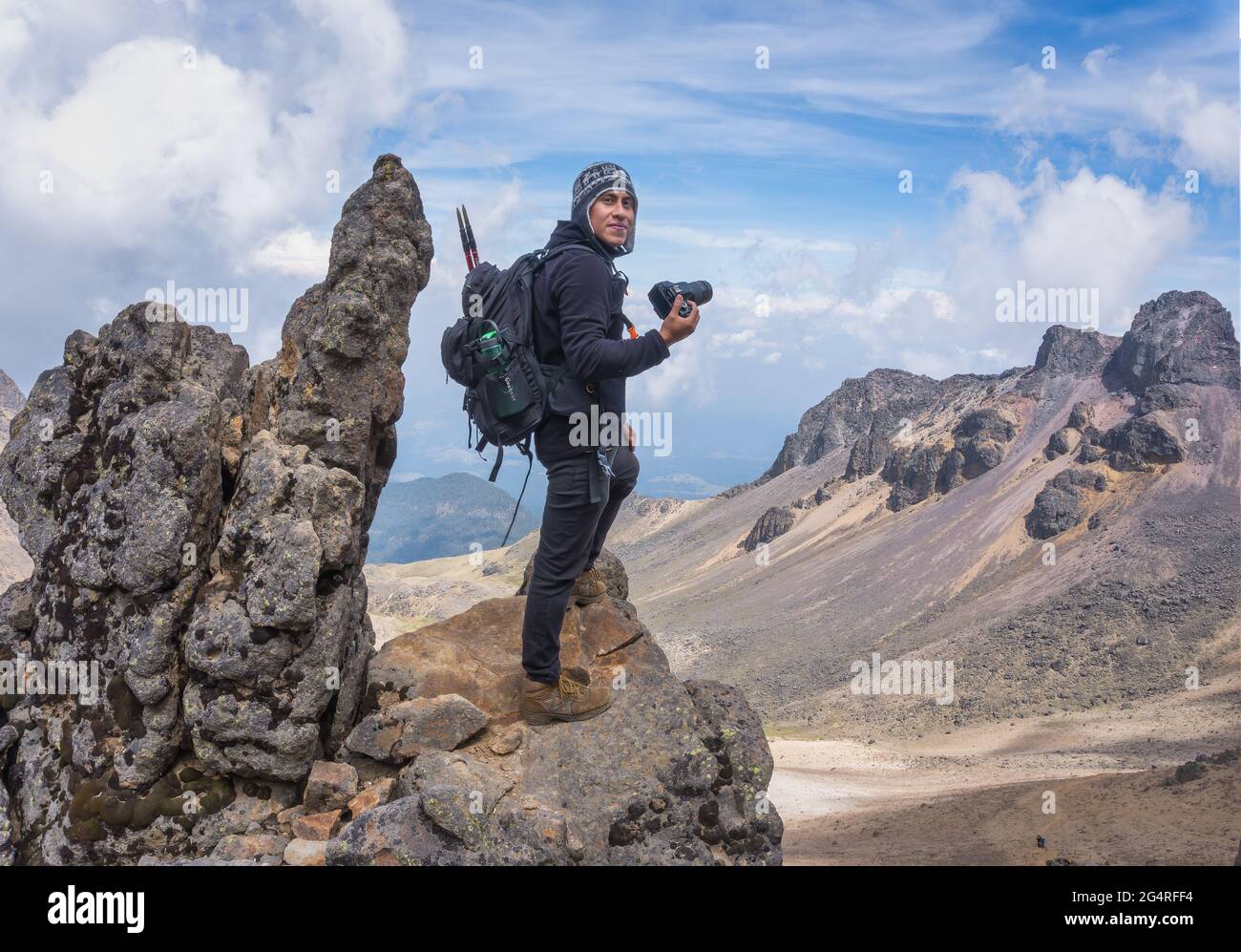 Smiling hispanic hiker with a professional camera on a camera on top of ...
