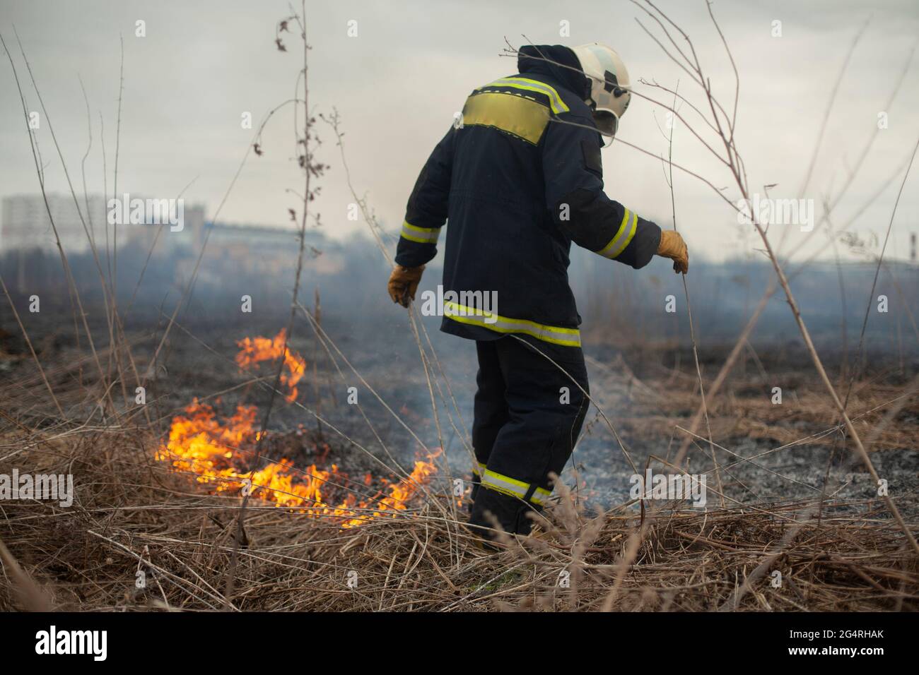 A firefighter extinguishes dry grass. A firefighter is fighting a fire ...