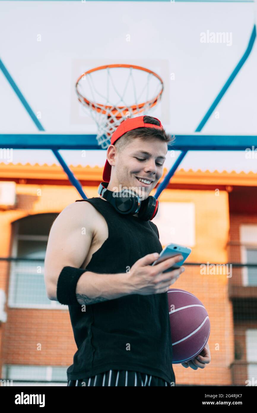 Attractive guy basketball player with a ball looks at his mobile phone ...
