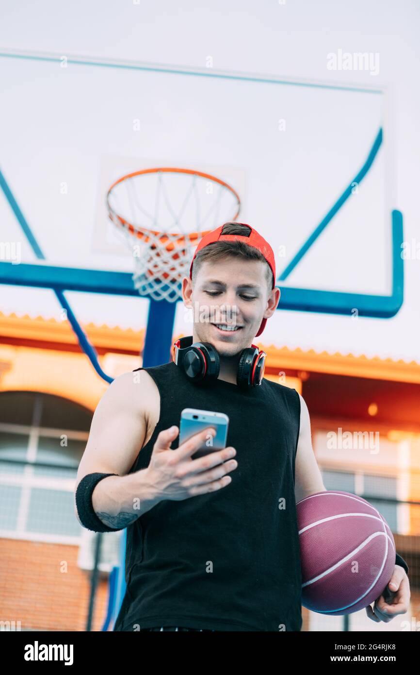 Attractive guy basketball player with a ball looks at his mobile phone ...