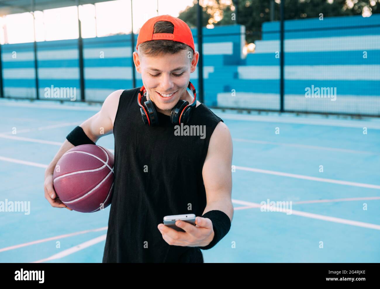 Attractive guy basketball player with a ball looks at his mobile phone ...