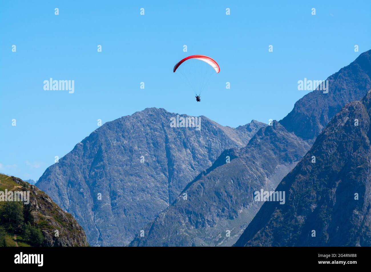 Paraplaners in tandem gliding in blue sky with view on Alpine mountains ...