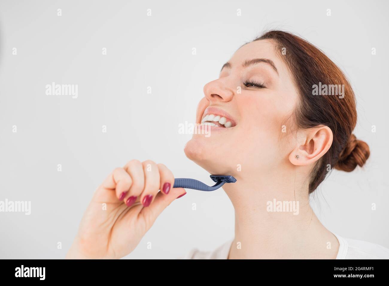 Caucasian funny woman shaves her face with a straight razor on a white ...