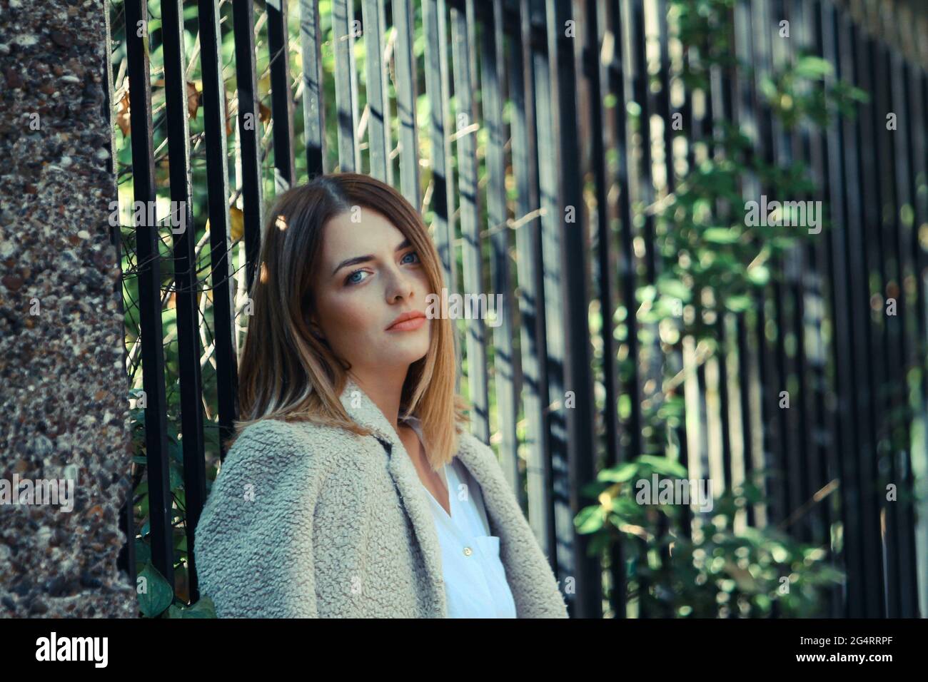 Shallow focus shot of a Caucasian female standing in front of a fence ...