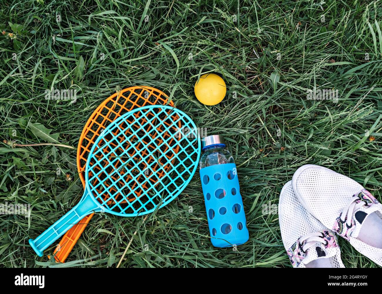 summer flat lay on green grass with rackets and ball, glass bottle of ...