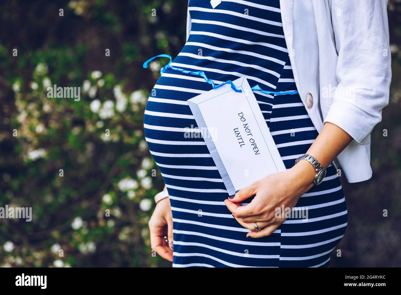 Closeup of a pregnant belly with a blue ribbon and a tag saying do not ...