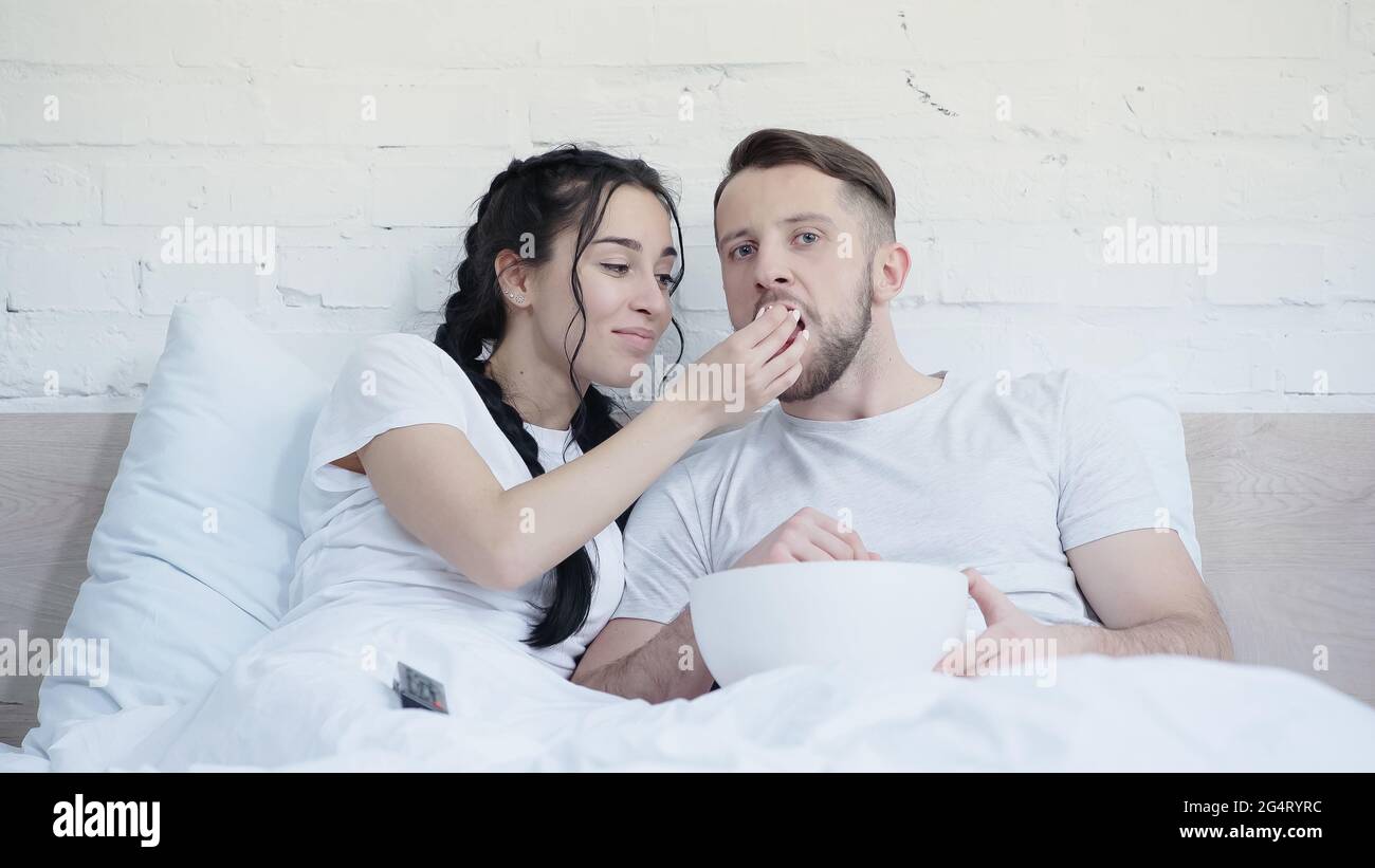 happy young couple eating popcorn and watching movie in bed Stock Photo ...