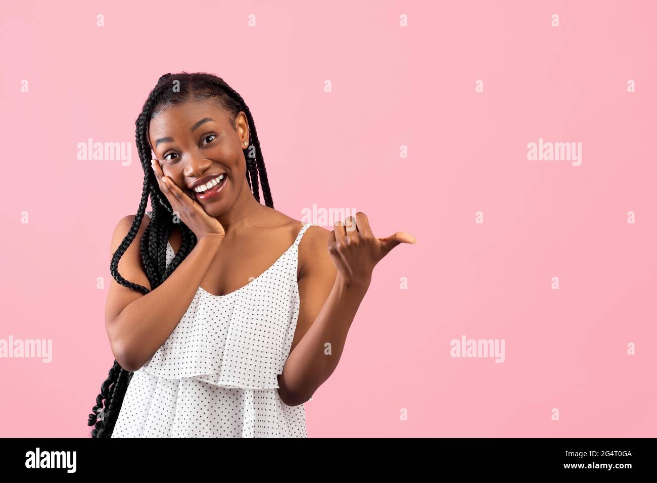 Joyful black lady pointing at blank space, touching her face in ...