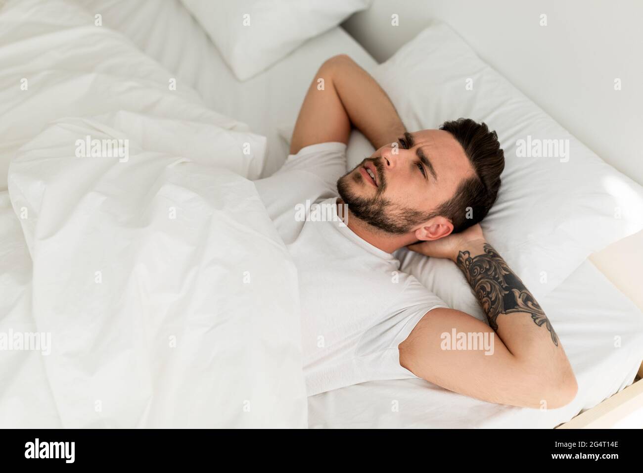 Angry young man unable to sleep, having insomnia, lying in bed and ...