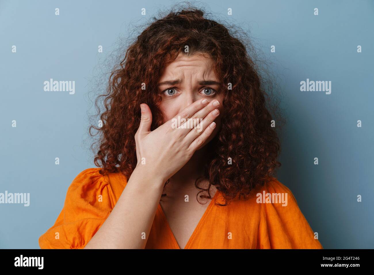 Unhappy ginger woman grimacing and covering her mouth isolated over ...