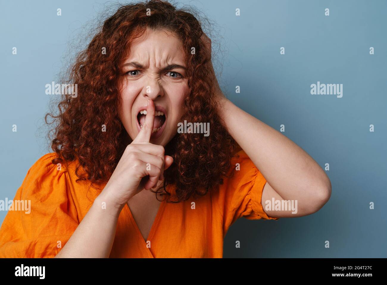 Furious ginger woman screaming while showing silence gesture isolated over blue background Stock ...