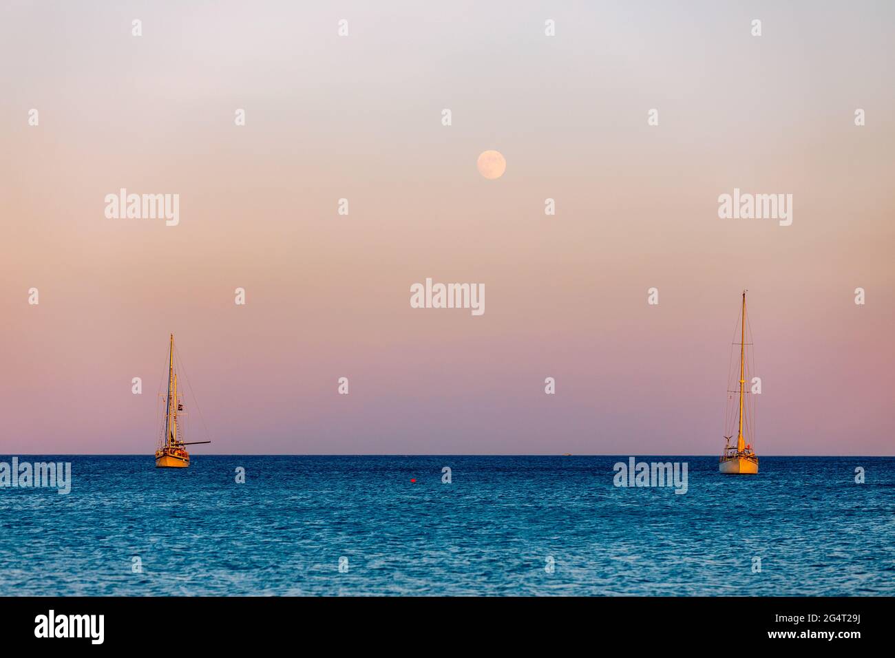 Full moon rising over the water with a small sailing boat in the ...