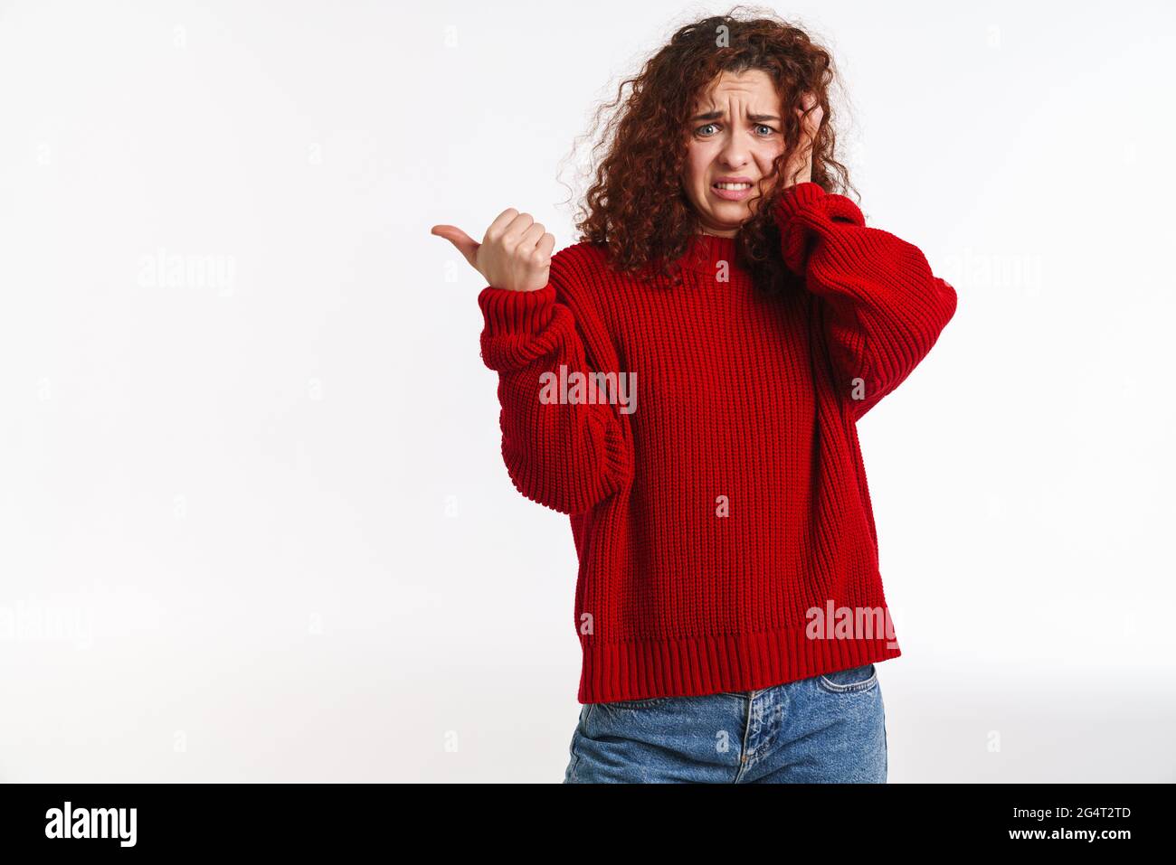 Scared ginger girl holding on her head and pointing finger aside ...