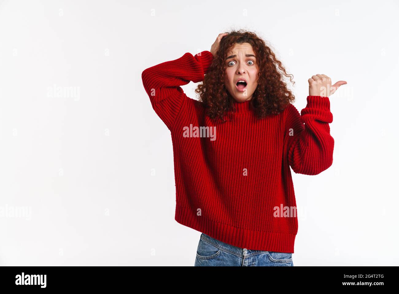 Shocked ginger girl holding on her head and pointing finger aside ...