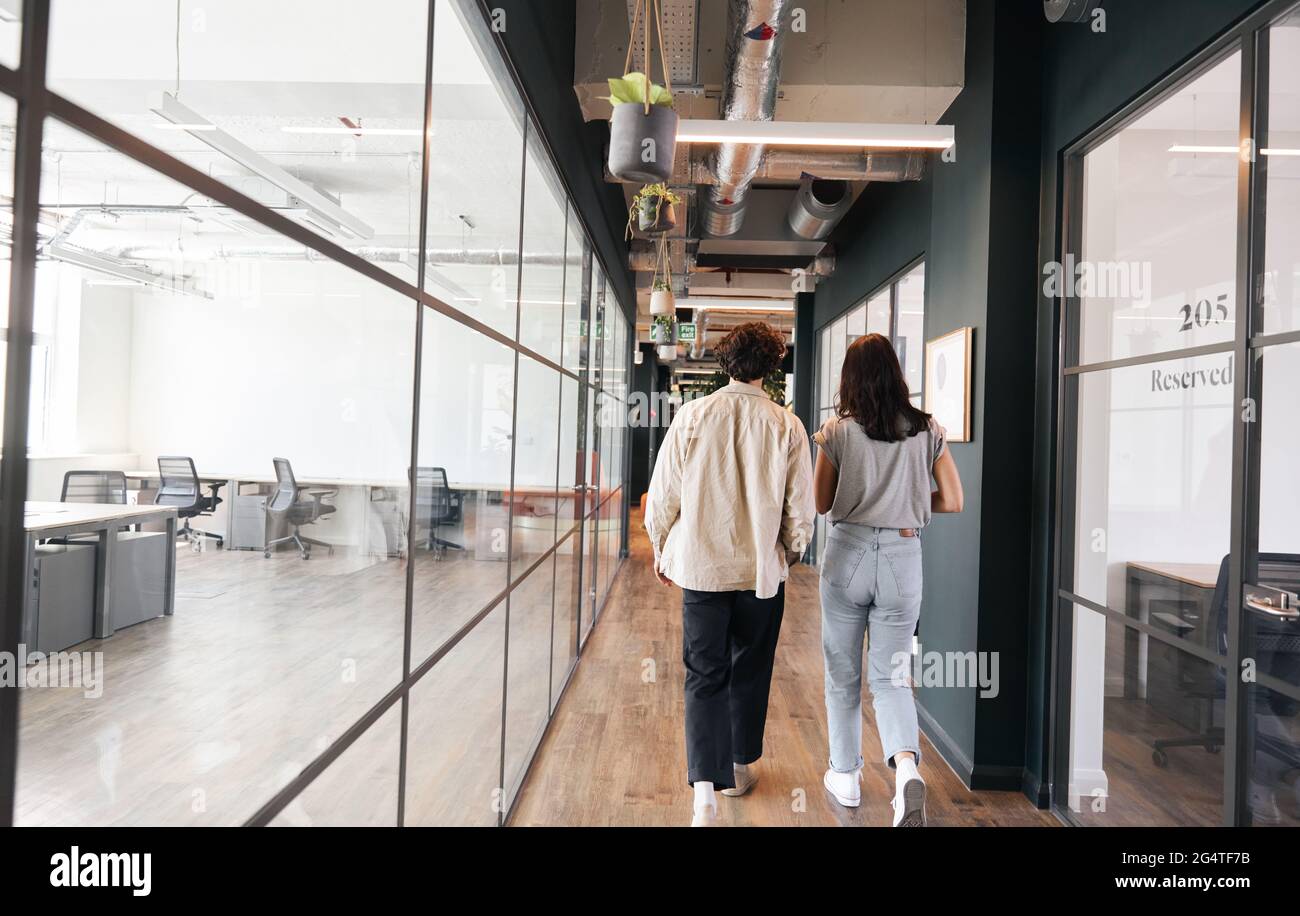 Rear view of young couple walking to office along walkway of modern ...