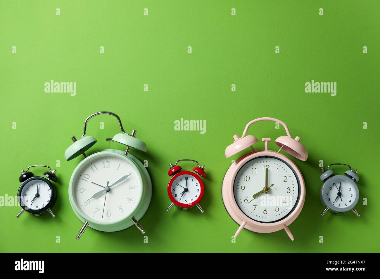Different multicolor alarm clocks on green background Stock Photo - Alamy